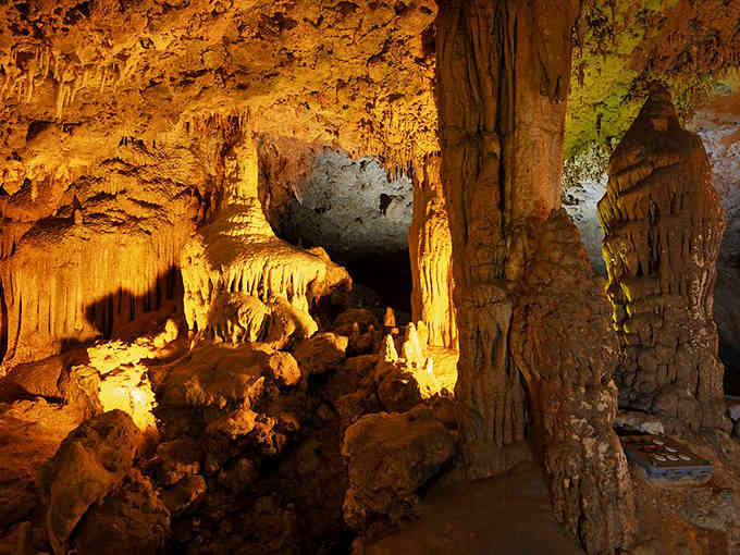 Golden stalactites hang like frozen honey in this underground chamber, lit dramatically to showcase millions of years of formation.
