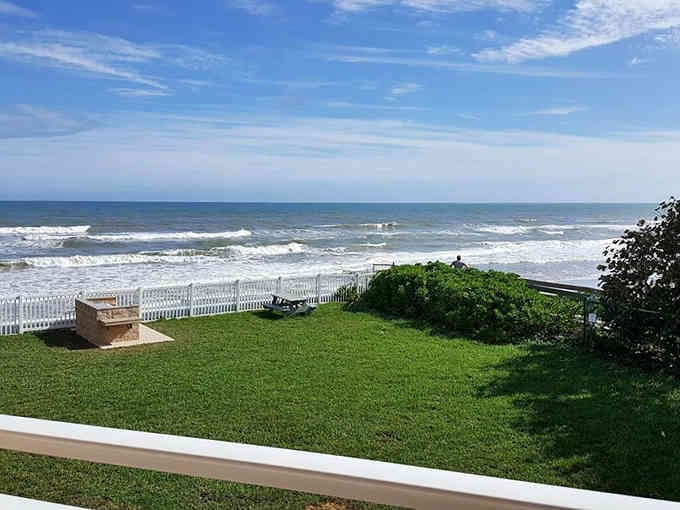 Ocean waves roll onto a pristine lawn where the grass meets the sea, creating the ultimate backyard for those lucky enough.