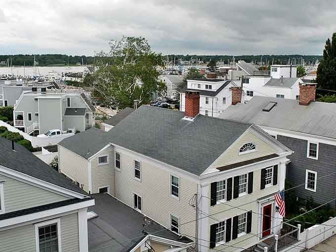 Classic homes overlook the harbor where sailboat masts create a forest of vertical lines against horizontal water views.