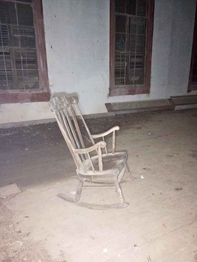 A solitary rocking chair waits on dusty floorboards, as if someone just stepped away for a moment.