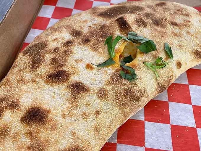 The golden-brown calzone with its perfectly blistered crust promises molten cheese and savory fillings waiting inside.