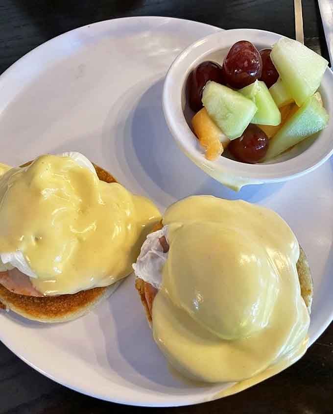 Silky hollandaise draped over poached eggs like a luxurious blanket, paired with fresh fruit for breakfast perfection.