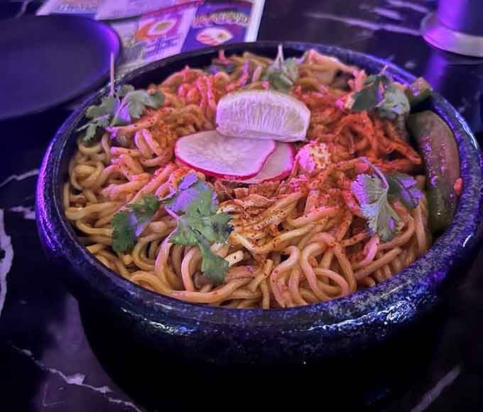 Spicy garlic noodles arrive in a dramatic black bowl, their tangle of flavors ready to wake up every taste bud you have.