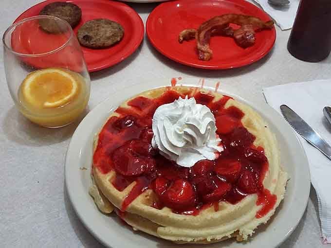 That strawberry waffle with whipped cream sits next to breakfast meats like dessert crashed the morning party and stayed.