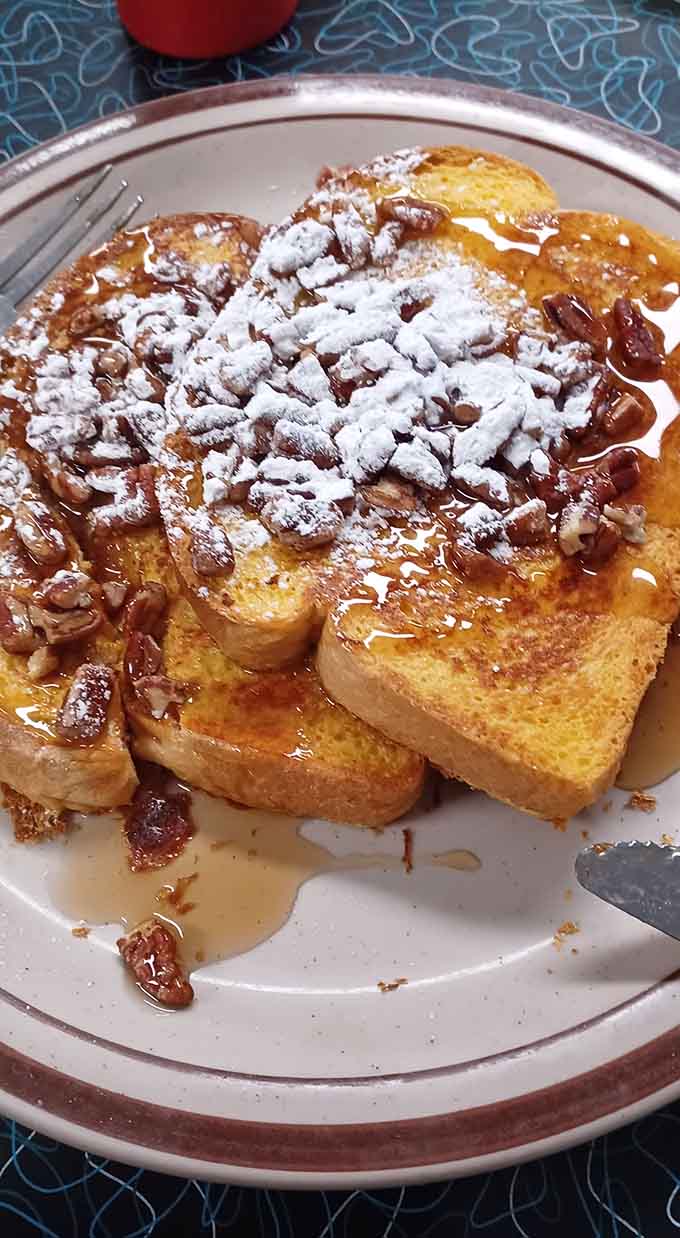 French toast drowning in syrup and pecans, dusted with powdered sugar like edible snow on breakfast mountains.