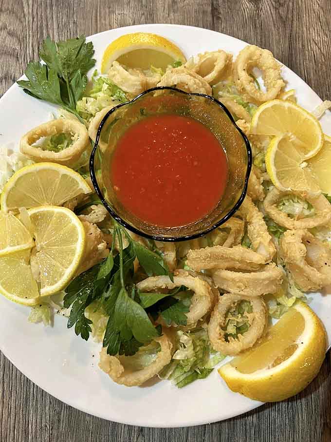 Golden calamari rings arranged like edible jewelry, with lemon wedges standing guard and cocktail sauce at the ready.