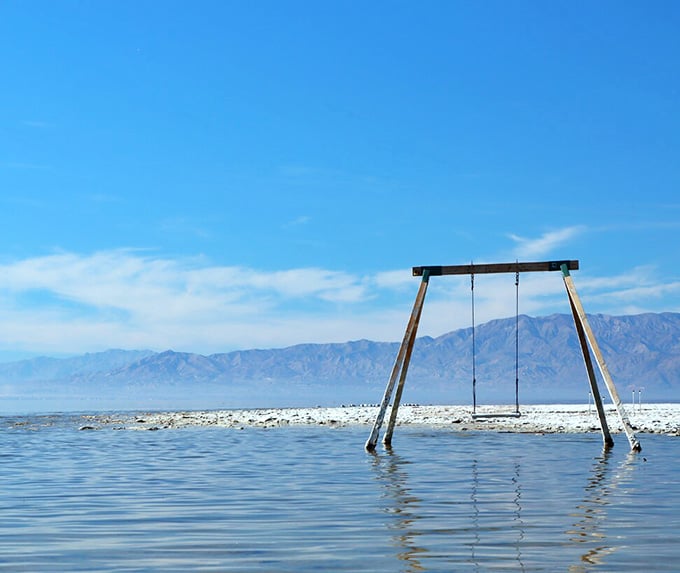 That lonely swing set stands as a monument to optimism, waiting for swimmers in waters that tell a different story.