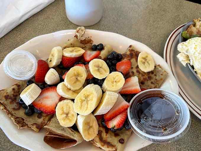 Fresh fruit and banana slices piled on crepes like edible confetti celebrating your excellent breakfast decision-making skills.