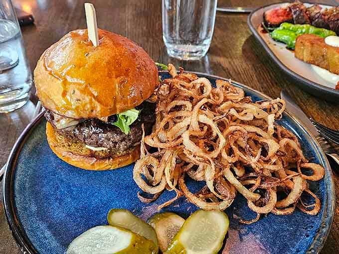 The burger arrives with crispy onion strings piled high, because sometimes excess is exactly what's needed.