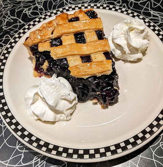 Lattice-topped blueberry pie with whipped cream, the kind of slice that makes you forget about your diet.