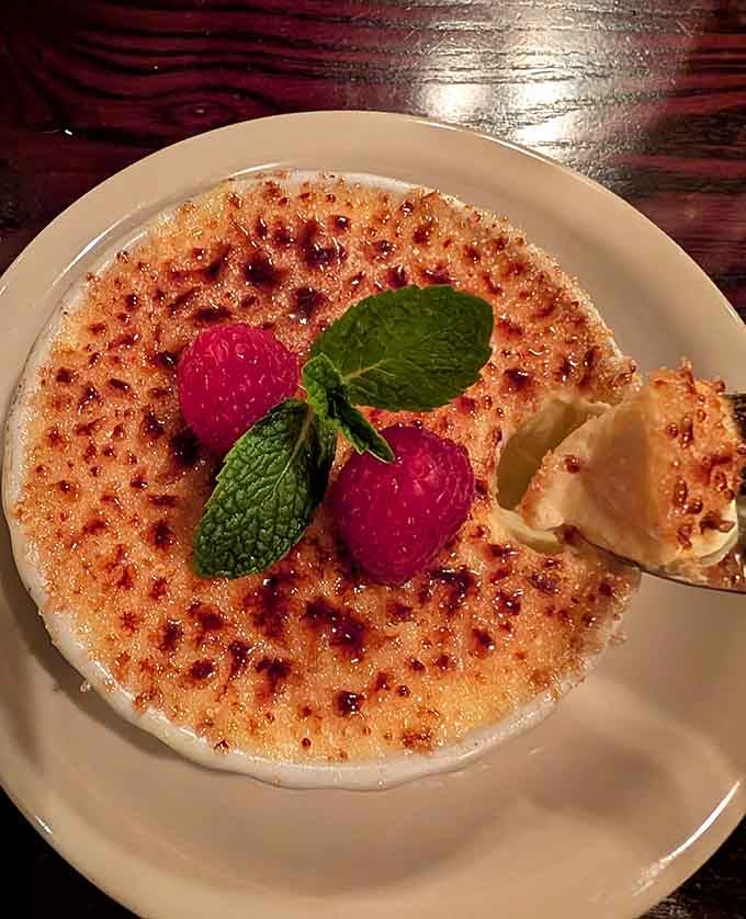 Caramelized sugar crackles under your spoon to reveal silky custard beneath, topped with fresh raspberries and mint.