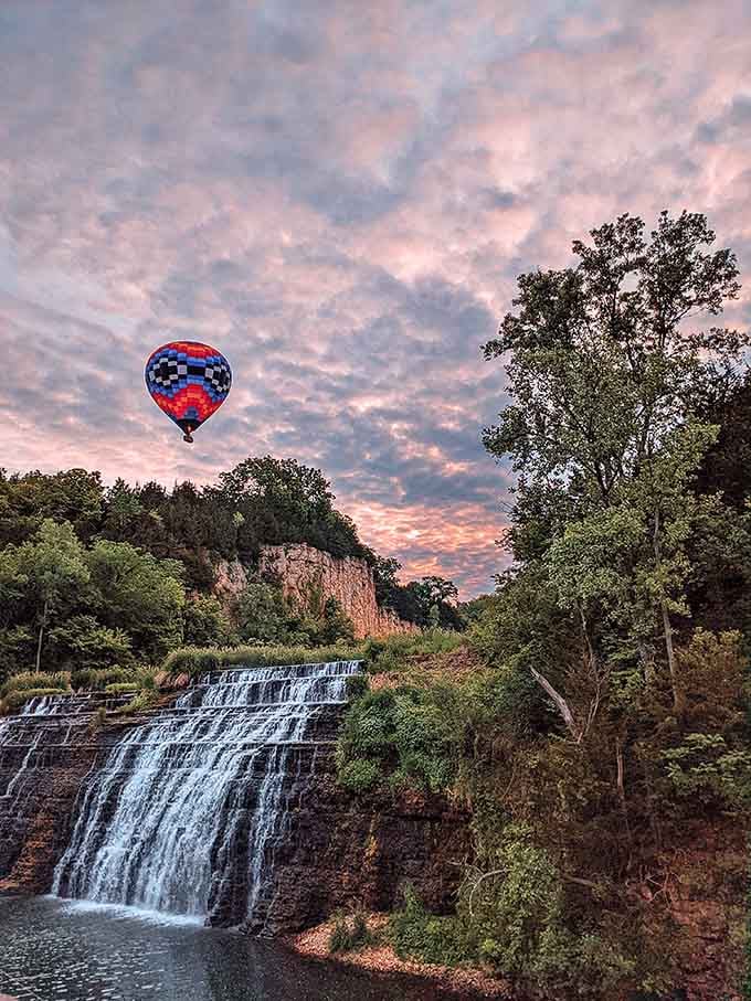 A hot air balloon drifting past at sunset turns this waterfall scene into something from a storybook illustration.