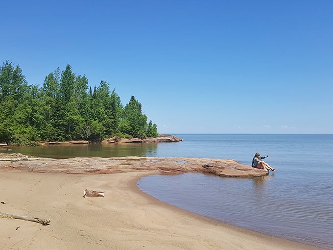 Red sandstone meets calm waters where beachcombing becomes meditation and time slows to lake speed.