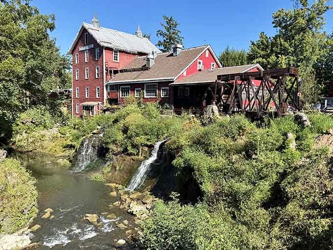 The historic red mill stands proud beside tumbling waters like old friends who've weathered centuries together.