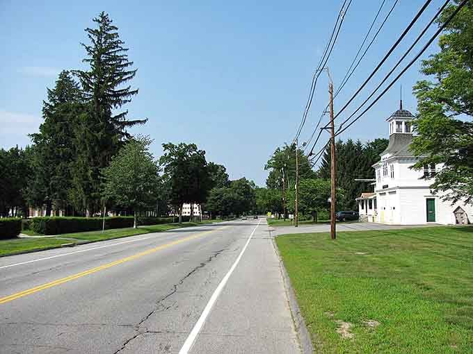 Sunny South Lancaster welcomes you with its quiet streets, historic white buildings, and lush green trees lining the peaceful road.