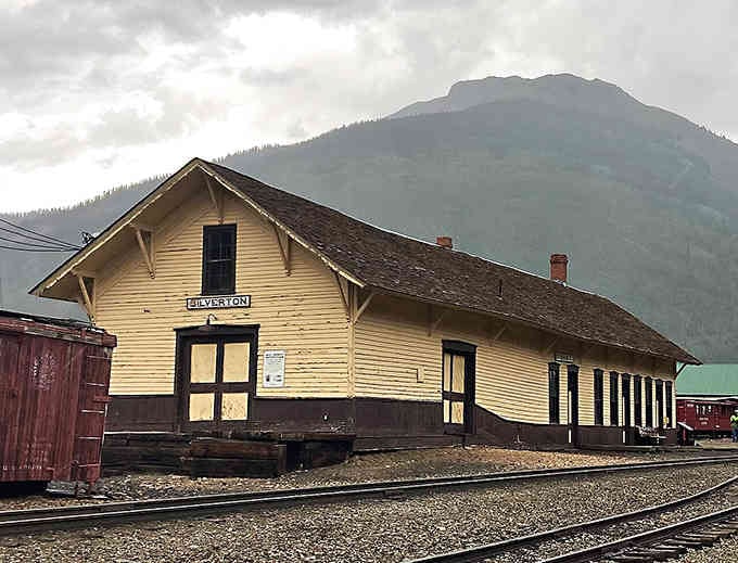 The old railroad depot stands weathered but dignified, a yellow sentinel to the days when trains brought the world to town.