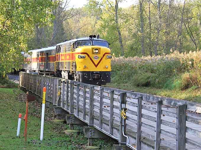 That sunshine-yellow locomotive crossing the wooden trestle looks like a vintage postcard sprung to life.