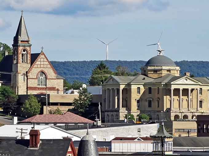 Historic church spires meet modern wind turbines in this mountain skyline where past and future shake hands daily.