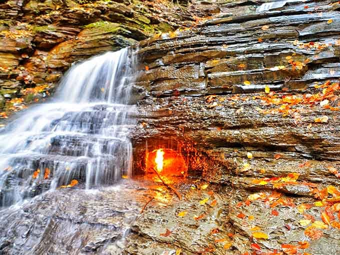 Nature's impossible magic trick glows behind cascading water, where autumn leaves frame fire meeting its ancient nemesis.