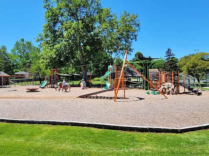 The vibrant playground sprawls beneath mature trees, creating that perfect blend of adventure and natural shade every parent dreams about.