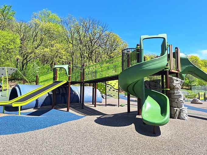 Green slides cascade from elevated platforms where accessibility meets adventure under Minnesota's brilliant blue sky.