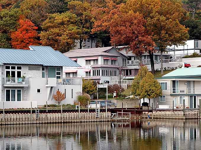 Waterfront homes nestle against autumn's blazing backdrop, their reflections doubling the beauty in Saugatuck's calm harbor waters.