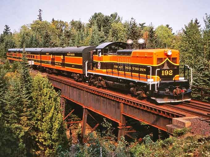 That orange and black locomotive crossing the trestle looks like it escaped from a vintage postcard's wildest dreams.