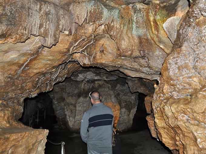 A visitor pauses to admire the intricate ceiling formations, where layers of colorful minerals tell stories of ancient geological processes.