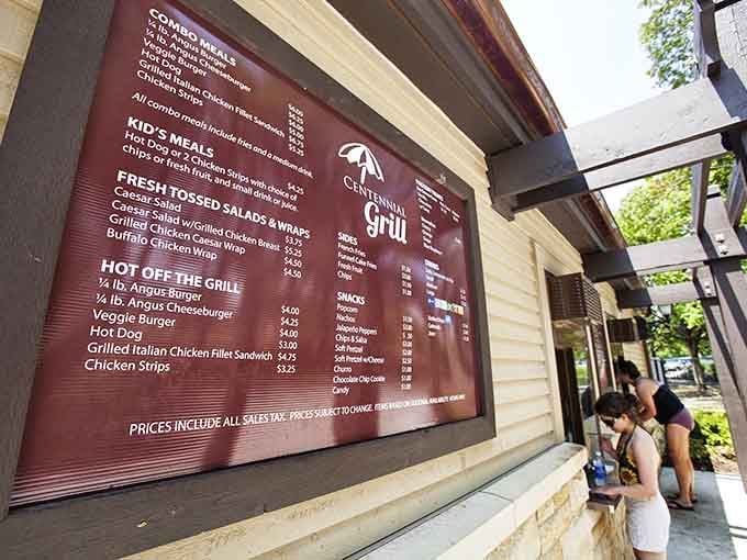 The Centennial Grill menu board promises classic poolside fare that tastes exponentially better when you're dripping wet and genuinely hungry from swimming.