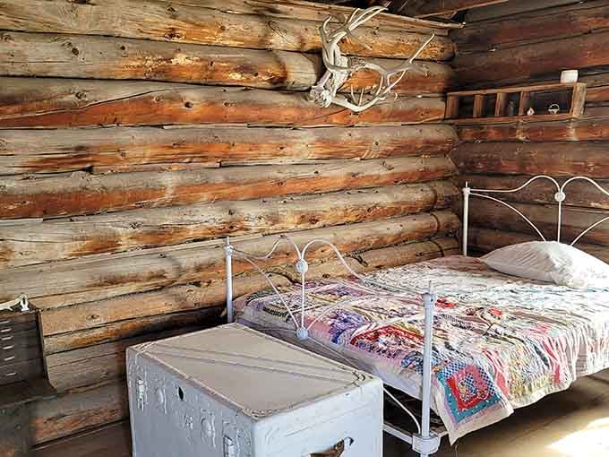 A metal bed frame and handmade quilt in a log cabin that housed entire families, no walk-in closets required.
