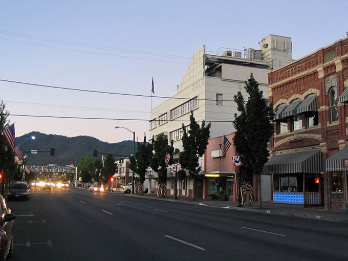 At dusk, downtown Grants Pass glows warmly, flags flying, mountains watching, the whole scene quietly magnificent and completely unhurried.