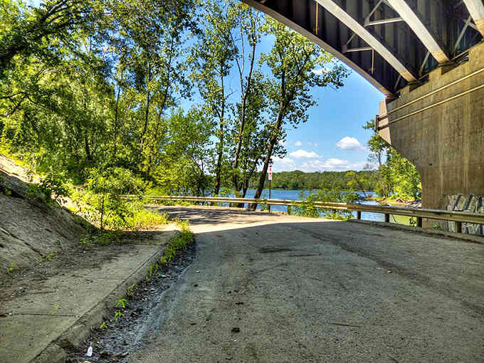 The path less traveled leads to riverside discoveries, where nature and infrastructure coexist in surprising harmony beneath the bridge.