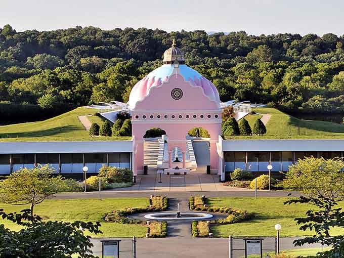 Expansive grounds showcase unique pink-domed structure nestled harmoniously within rolling green landscape and forest backdrop.