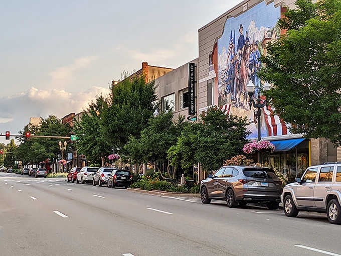 Evening light softens the streetscape as the patriotic mural glows, while mature trees frame a downtown that honors its roots.