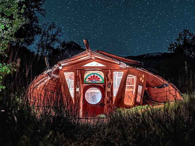 The night sky transforms this whimsical dwelling into something from a fairytale, glowing warmly against star-studded darkness.