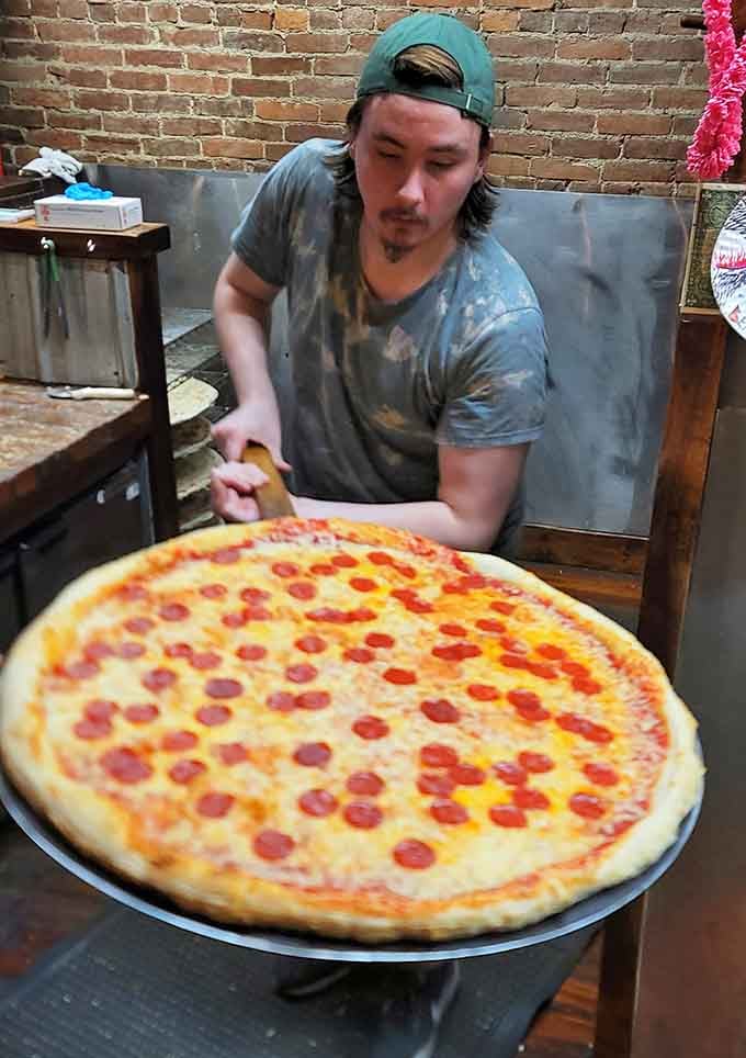 The proud creator holding a pepperoni masterpiece that probably weighs more than most newborn babies, and that's not hyperbole.