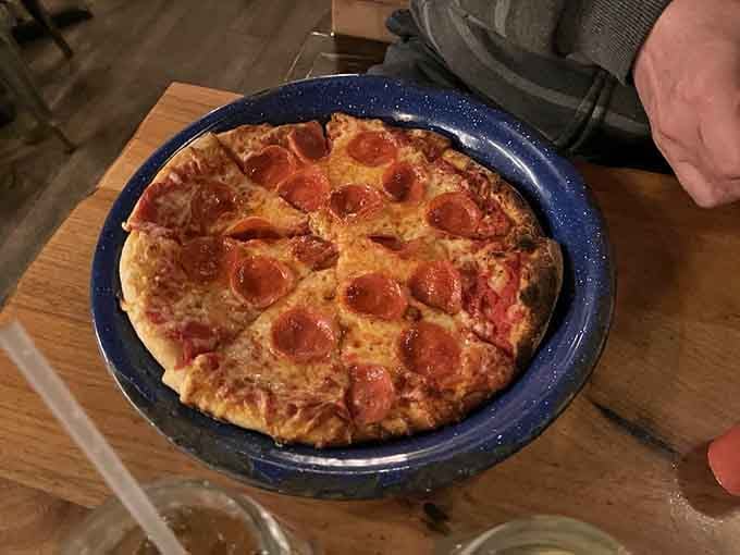 Pizza served on a speckled camping plate, because even Italian food gets the outdoor treatment here. It works beautifully.