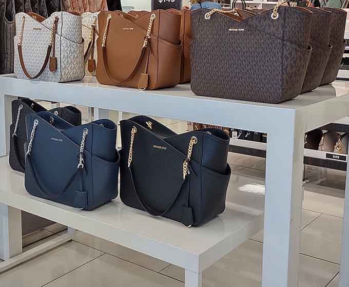 Michael Kors bags lined up like soldiers ready to elevate your entire wardrobe without destroying your credit score.