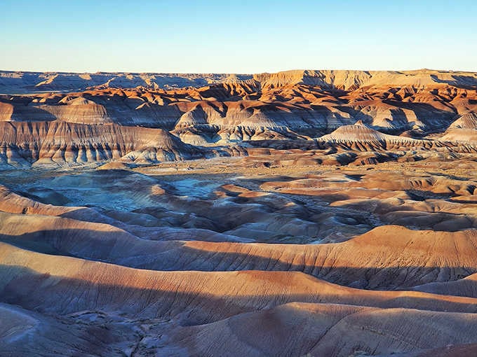 Vibrant layers of sun-kissed clay badlands invite you to marvel at nature's stunning, colorful canvas stretching across the horizon.