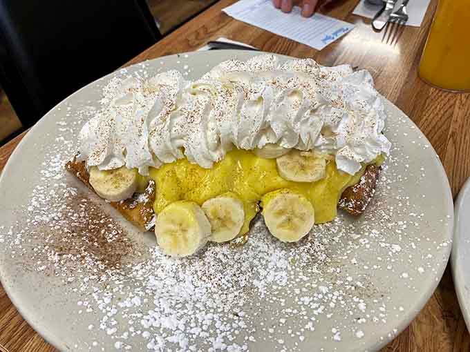 Banana slices peeking through clouds of whipped cream on this waffle create a dessert experience that transcends traditional breakfast boundaries.