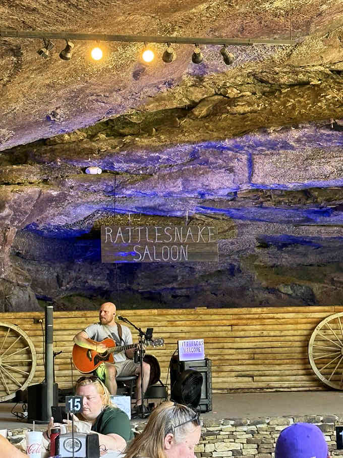 Live music echoes off limestone walls as a guitarist strums beneath purple stage lights, turning geology into an intimate concert venue.