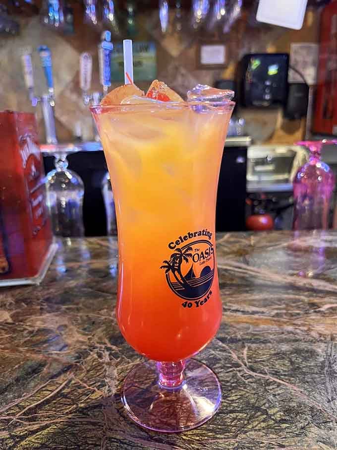 A tall, sunset-colored cocktail served in a branded glass, because some drinks deserve their own souvenir moment.