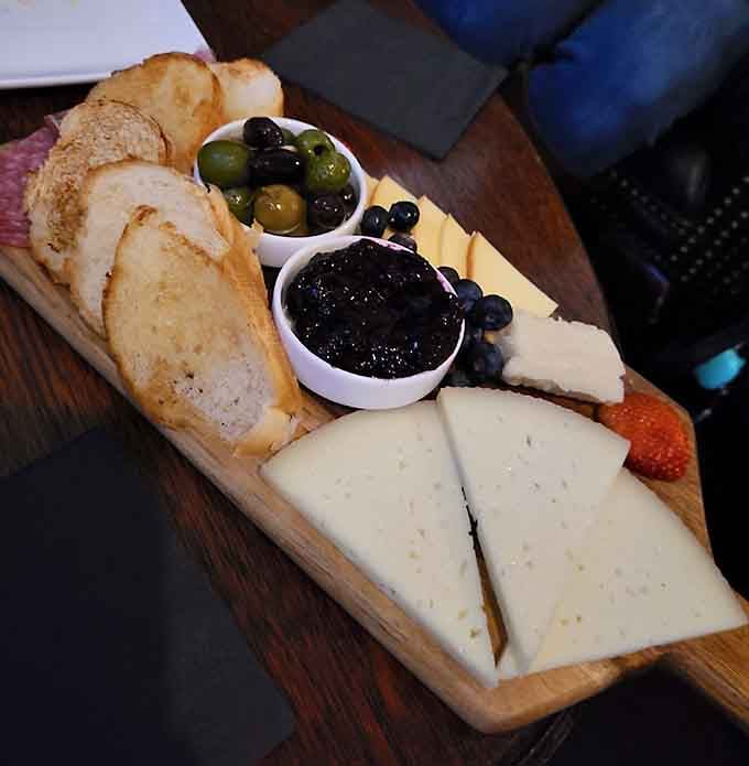 Crusty bread, artisan cheese, and jewel-toned preserves arranged like edible architecture on weathered wood, simply stunning.