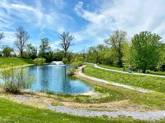 Spring green surrounds this tranquil pond where families gather, ducks paddle lazily, and the fountain creates its own soothing soundtrack for relaxation.
