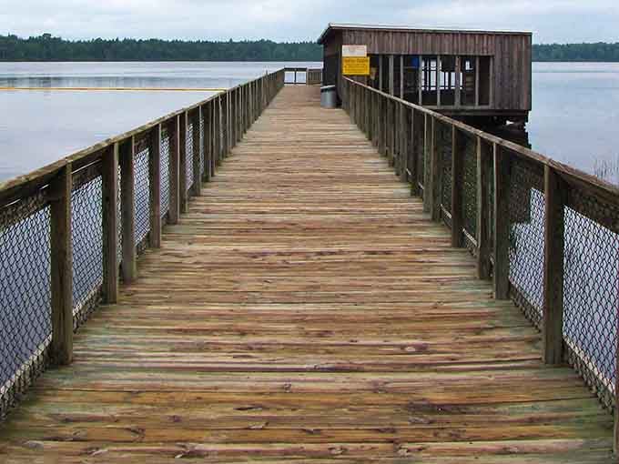 This weathered boardwalk stretches toward quiet contemplation, where fishing poles and peaceful thoughts find equal welcome at water's edge.