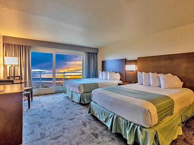 Two beds face floor-to-ceiling windows framing the Pacific sunset, making every morning feel like a vacation commercial.