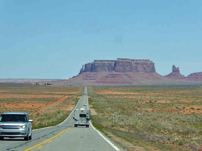 Modern vehicles meeting ancient geology on a highway that connects past, present, and your vacation plans perfectly.