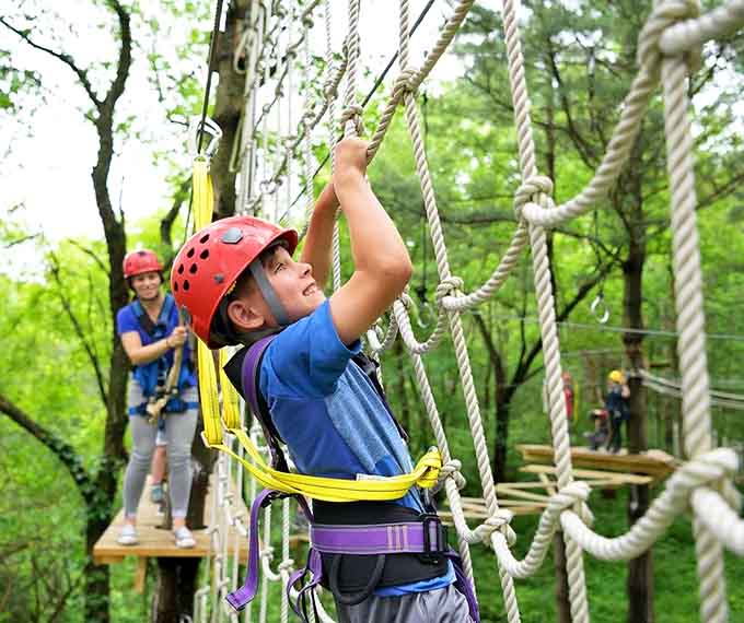Gripping ropes overhead, this young adventurer demonstrates the concentration required for aerial obstacle navigation success.