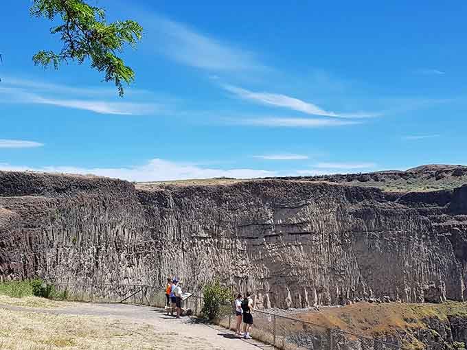Visitors reading interpretive signs while columnar basalt towers behind them like nature's own architectural blueprint.