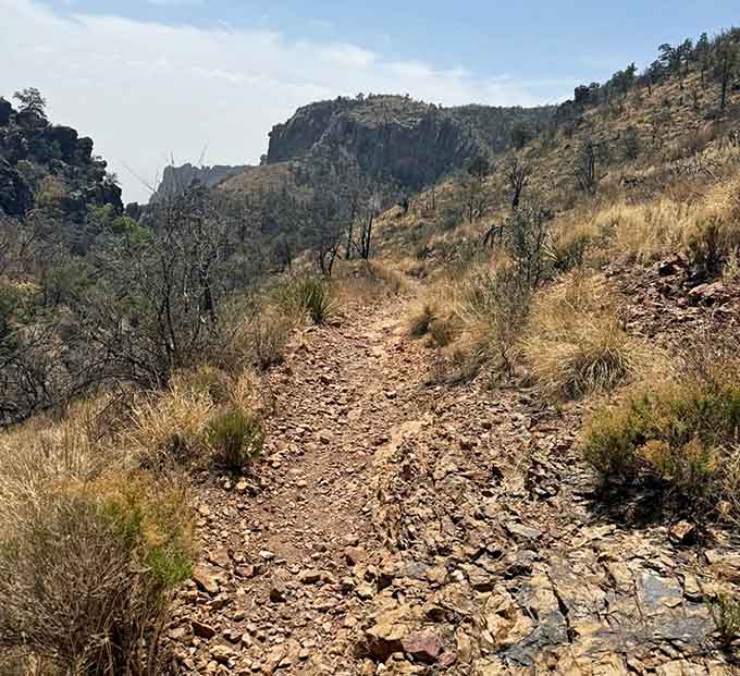 The rocky path winds through golden grasses, leading hikers deeper into terrain that feels wonderfully remote and untamed.